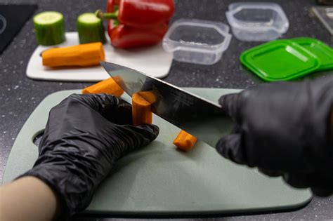 날카로운 칼로 도마에 신선한 당근을 자르고 위생을 보장하는 검은 장갑을 끼고 배경에 오이와 빨간 피망을 넣습니다 건강한 생활방식에 대한 스톡 사진 및 기타 이미지 Istock