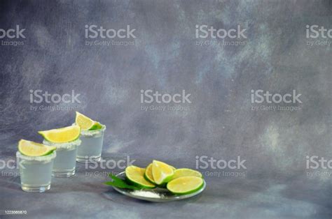 소금 결정에 가장자리와 라임 조각 의 상단에 감귤류조각과 회색 배경에 소금 의 핀치와 함께 유리 접시 위에 데킬라 의 세 잔 3가지 개체에 대한 스톡 사진 및 기타 이미지