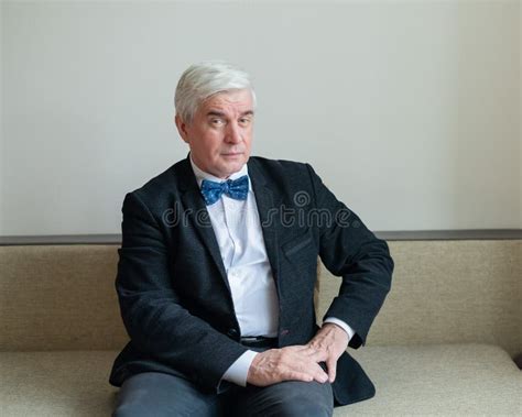Confident Elderly Gray Haired Business Man In A Suit And Bow Tie Sits