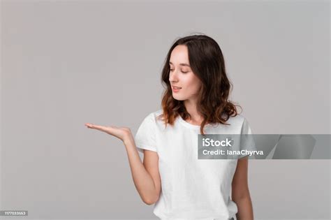 회색 배경 위에 고립 된 제품 배치를위한 빈 공간이있는 손바닥을 들고흰색 티에 예쁜 갈색 머리 여자 광고 의 공간을 복사합니다 T 셔츠에 대한 스톡 사진 및 기타 이미지