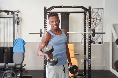 Man With Glasses Looking At Camera While Exercising With Dumbbells At The Gym Stock Photo