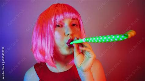 Woman In A Bright Pink Wig At A Party She Is Blowing At A Party Horn