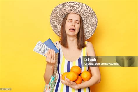 줄무늬 원피스 수영복과 밀짚모자를 쓴 슬픈 우는 여자는 노란색 배경 위에 고립된 포즈를 취하고 과일 여권 서류를 손에 들고 화를 내고 있다 30 34세에 대한 스톡 사진 및