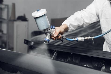 마스크를 쓰고 페인트 챔버에서 자동차의 일부를 그리는 보호 작업복을 입은 자동차 수리공 화가의 장면을 닫습니다 검은색에 대한