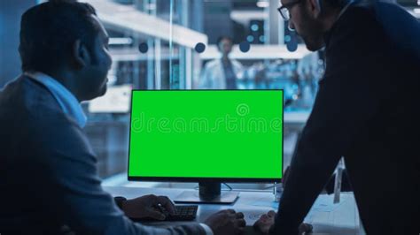 Two Developers Working On Computer With Green Screen Mock Up Display