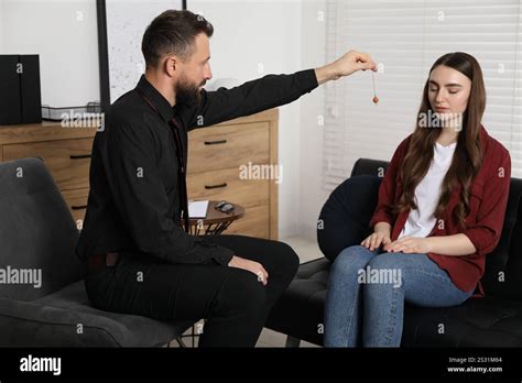 Psychologist using pendulum while working with patient during hypnosis session indoors Stock ...