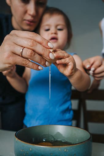 어린 어머니는 어린 딸에게 계란을 그릇에 부수고 집에서 함께 음식을 준비하는 법을 보여줍니다 아이에게 요리를 가르치는 어머니 개념 가족 활동 디저트 학습 가족 사랑 활동