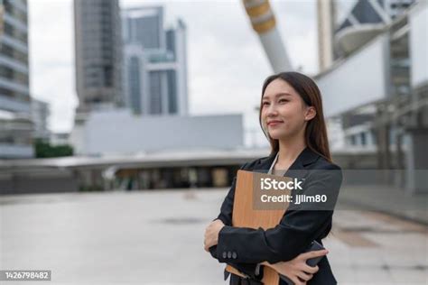 방콕 시내의 중심 비즈니스 지구에서 클립 폴더 보드와 스마트 폰을 들고 하늘을 올려다 보는 자신감있는 미소를 짓는 매력적인 젊은 아시아 전문 사업가 여성 위를 보기에 대한