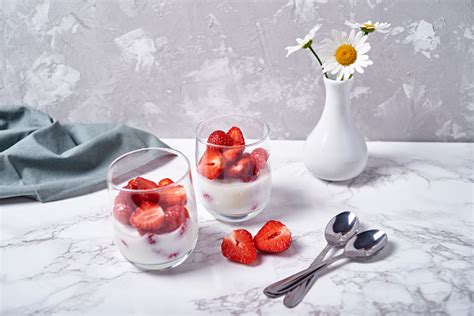 신선한 슬라이스 딸기 숟가락 꽃병에 카모마일 꽃과 흰색 대리석 배경에 테이블 냅킨건강한 요구르트 의 두 안경 복사 공간 건강한 아침 식사 음식 개념 0명에 대한 스톡 사진
