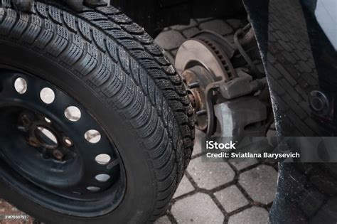 자동차 타이어 교체가 진행 중입니다 검은 장갑을 낀 사람이 차량 근처에서 제거된 휠을 만지고 있어 노출된 브레이크 디스크와