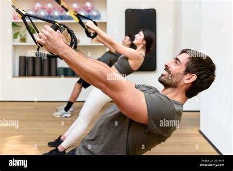 Side View Of Bearded Male Athlete Smiling And Doing Low Row Exercise With Trx Ropes During Group
