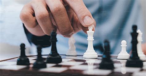 체스 게임 플레이어는 흰색 폰을 한 걸음 앞으로 움직입니다 파란색 배경에 보드에 체스 조각 체스맨은 체스를 두며 첫 번째 동작을 폰으로 만들고 손을 보여줍니다 사진