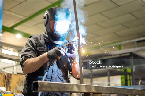 보호 마스크와 작업복을 입은 용접공으로 일하는 남자가 Migmag 용접기로 수직 작업을 수행합니다 중소기업에서 용접 작업 생산 1940 1949 년에 대한 스톡 사진 및