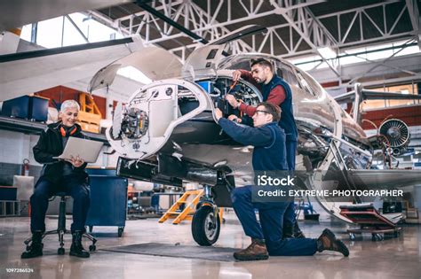 노인 여성 항공기 엔지니어 앉아서 격납고에서 작은 비행기에 일 손 도구를 사용 하는 그녀의 동료를 돕는 그녀의 노트북을 사용 하 여 항공우주 산업에 대한 스톡 사진 및 기타