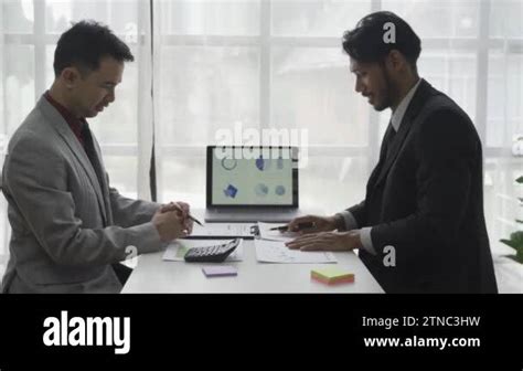 Asian Male Businessman With Two Financial Advisers Analyzing Chart Data In Document Use Files