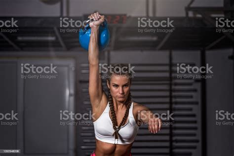 젊은 아름 다운 매력적인 근육과 강한 맞는 여자 들고 무거운 케틀벨 한 손으로 그녀의 머리 위에 스윙 또는 날치기 하드 코어 크로스 운동 훈련 에 체육관 실제 사람들 강사에