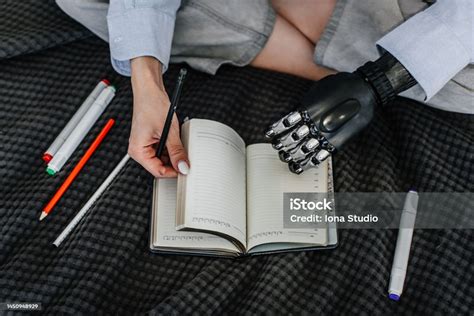 침대에 앉아 있는 여성의 자른 이미지는 생체 역학적 손을 사용하여 일기를 엽니다 집에서 인공 팔 계획 의제를 가진 소녀 외상 후 정형 외과 및 재활 의학 및 전자 제품 20