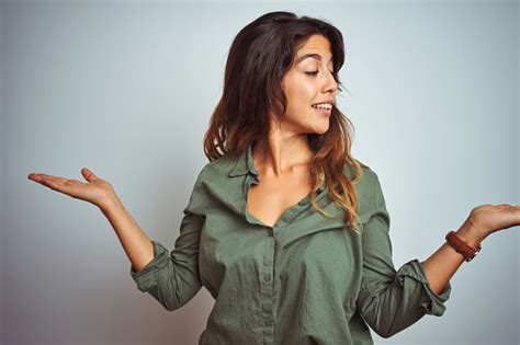 회색 고립 된 배경 위에 서있는 녹색 셔츠를 입은 젊은 아름다운 여성은 양손을 열고 손바닥을 보여주는 미소 제시 및 광고 비교 및 균형 갈색 머리에 대한 스톡 사진 및 기타