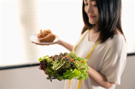 젊은 아시아 여성은 야채 샐러드와 정크 푸드 프라이드 치킨 을 손에 접시에 선택하는 체중을 잃고 다이어트와 좋은 건강 개념 개념에 대한 스톡 사진 및 기타 이미지 Istock