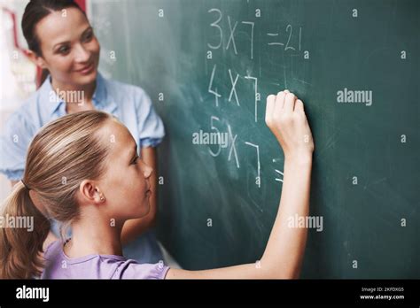 Mini Mathematician A Young Girl Doing Maths On The Board As Her Teacher Watches Smiling Stock