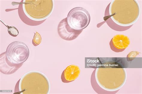 레몬 타히니 마늘 소금 물 한 잔을 그림자와 반사가 있는 고립된 파스텔 분홍색 배경에 반으로 자릅니다 미적 음식 개념입니다 플랫