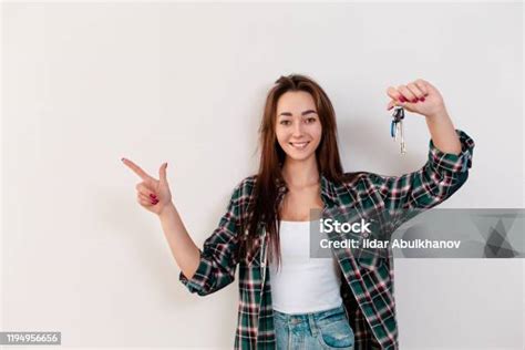 부동산 구매 및 임대 격자무늬 셔츠를 입은 미소 짓는 여성은 왼손에 오른손을 들고 열쇠와 포인트를 들고 있다 흰색 배경 및 복사 공간 가정 생활에 대한 스톡 사진 및 기타