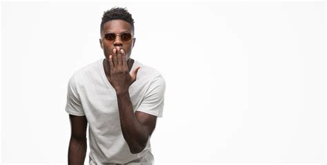 침묵 비밀 개념에에서 무서 워 하는 젊은 아프리카계 미국인 남자가 손으로 착용 선글라스 커버 입 실수 두려움의 표현에 대 한