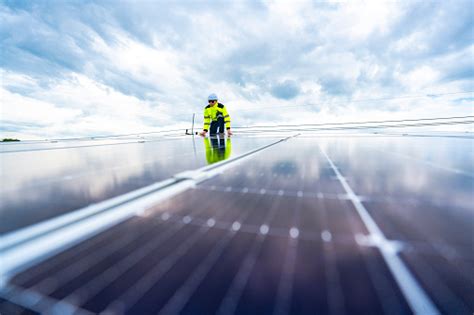 숙련된 기술자가 옥상에 설치된 태양 전지판을 조정하여 지속 가능한 에너지로의 전환을 강조합니다 안전 장비를 착용한 작업자는 재생 에너지 설비에서 정밀성을 보여줍니다 건설