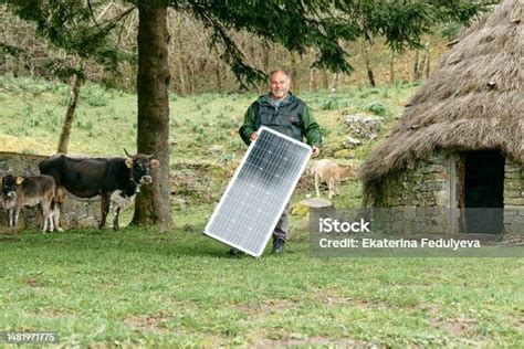 농촌의 농장 오두막과 소들 근처에서 태양 전지판을 들고 있는 중년의 수염 난 남자 대체 에너지 재생 가능 에너지원 및 지속 가능한 에너지 자원 개념 60 64세에 대한 스톡
