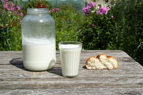 거리의 나무 테이블에는 2리터의 우유 캔이 서 있습니다 근처에는 양면 우유 한 잔과 흰 빵이 부서진 헌치백이 서 있습니다 건강한 생활방식에 대한 스톡 사진 및 기타 이미지