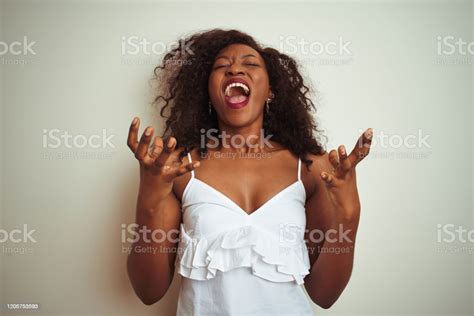 고립된 흰색 배경 위에 서있는 티셔츠를 입은 젊은 아프리카 계 미국인 여성은 공격적인 표정과 팔을 들고 미친 소리와 고함을 질렀습니다 좌절 개념입니다 T 셔츠에 대한 스톡