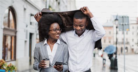 행복한 아프리카 계 미국인 남자와 여자는 도시 거리를 걷는 동안 재킷 아래 비를 피하고 숨어 있습니다 비즈니스 미팅에 참석하는 두 비즈니스 파트너 사진