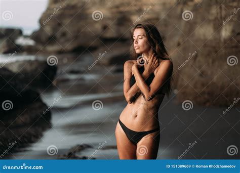 Brunette Girl In Black Swimwear Rests On Black Sand Beach Stock Image