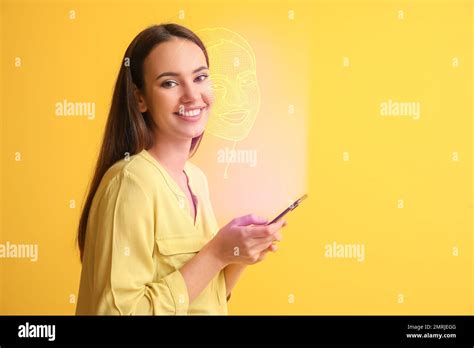 Young Woman With Mobile Phone Using Facial Recognition System On Yellow