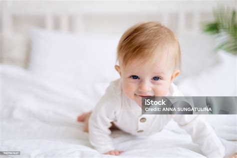 웃는 아기 6 개월 된 금발 소년은 아침에 면 바디 수트 어린이 용품의 개념에서 자고 난 후 밝은 침실의 흰색 침대에서 기어