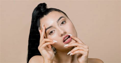 포니테일 헤어스타일을 가진 아름 다운 젊은 섹시한 아시아 여성 베이지 색 배경에 고립 된 얼굴 입술과 눈썹을 만지는 손으로
