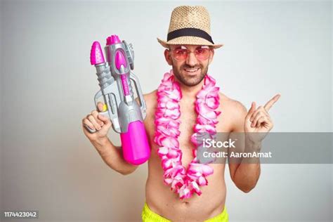 여름 모자를 쓰고 하와이 안 레이 꽃은 고립 된 배경 위에 물 총을 들고 매우 행복한 측면에 손과 손가락으로 가리키는 가리키기에