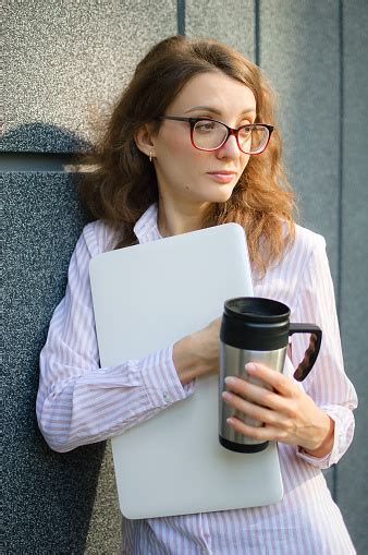 실버 노트북과 커피 한 잔을 가진 젊은 여성의 여성 초상화는 아침에 어두운 회색 벽 근처에서 회의를 기다리고 원격 작업 커피