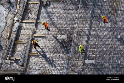 Construction Site Workers In Orange Uniform Carrying Steel Bars Rebars Floor Builders Working