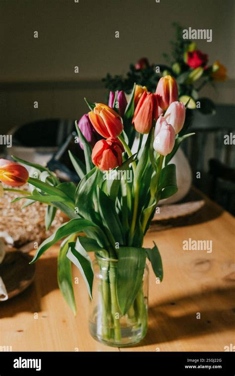 A Vase Of Tulips Sits On A Wooden Table The Tulips Are In Various