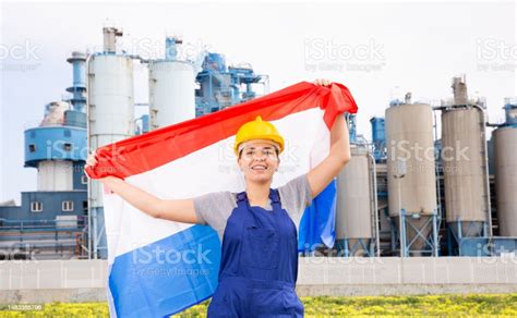 현대 공장의 굴뚝을 배경으로 네덜란드 국기를 손에 들고 작업복을 입은 긍정적인 소녀 20 24세에 대한 스톡 사진 및 기타 이미지 20 24세 30 39세 감정