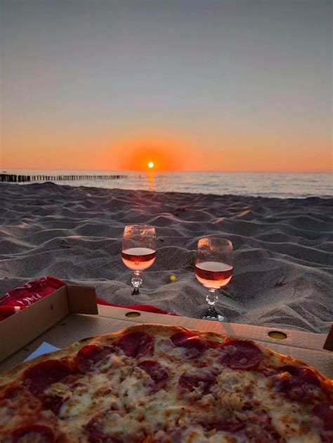 Two Glasses Of Wine And A Pizza On The Beach At Sunset With Water In