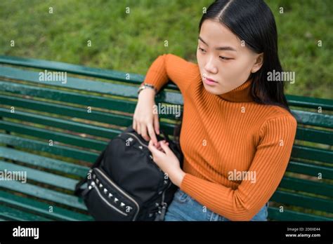 Portrait Of Young Beautiful Asian Woman Sitting On A Bench In The Park