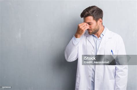 흰색 코트를 입고 회색 그런 지 벽에 잘생긴 젊은 전문 남자 피곤 바르고 코와 눈 피로 두통 느낌 스트레스와 좌절 개념입니다 건강관리와 의술에 대한 스톡 사진 및 기타