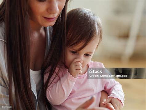 Joven Madre Jugando Con Su Curiosa Hija Bebé Chupando Su Pulgar En Casa Mamá Y Niña Mirando Algo