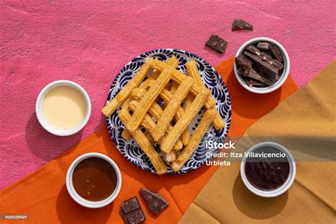 테이블에 츄러스가 있는 분홍색 배경 플레이트 츄러스가 있는 접시의 평면도 흰색 세라믹 그릇에 다양한 토핑 근처의 테이블