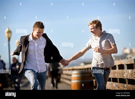 Two Smiling Young Homosexual Men Running Together While Holding Hands