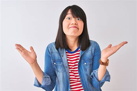 데님 셔츠와 빨간 줄무늬 티셔츠를 입은 중국 여성은 고립된 흰색 배경에 팔과 손을 들고 혼란스러운 표정을 짓고 있다 의심 개념 아시아인에 대한 스톡 사진 및 기타 이미지