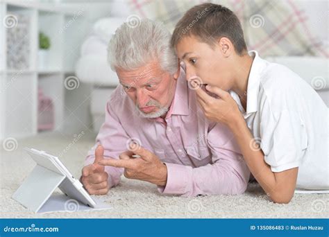Grandfather With Grandson Using Tablet While Lying On Floor Stock Image