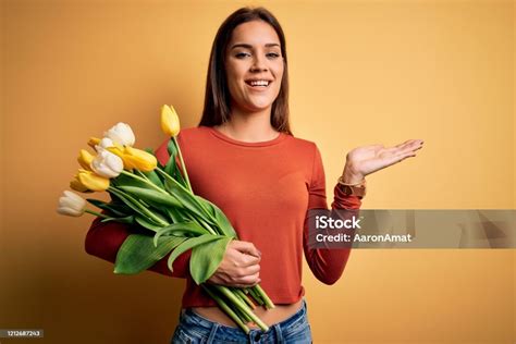 젊은 아름 다운 갈색 머리 여자 노란 배경 에 튤립 꽃다발을 들고 쾌활 한 제시 하 고 카메라를 보고 손바닥으로 가리키는 미소 가리키기에 대한 스톡 사진 및 기타 이미지